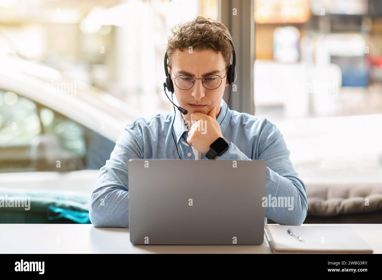 Serious, focused, busy young european guy in glasses, headphones using ...
