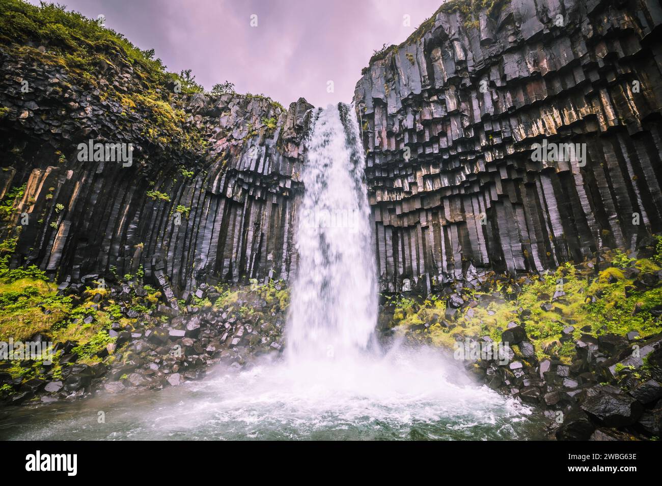 Masses of water cascade down the Skaftafell waterfall along gray basalt ...