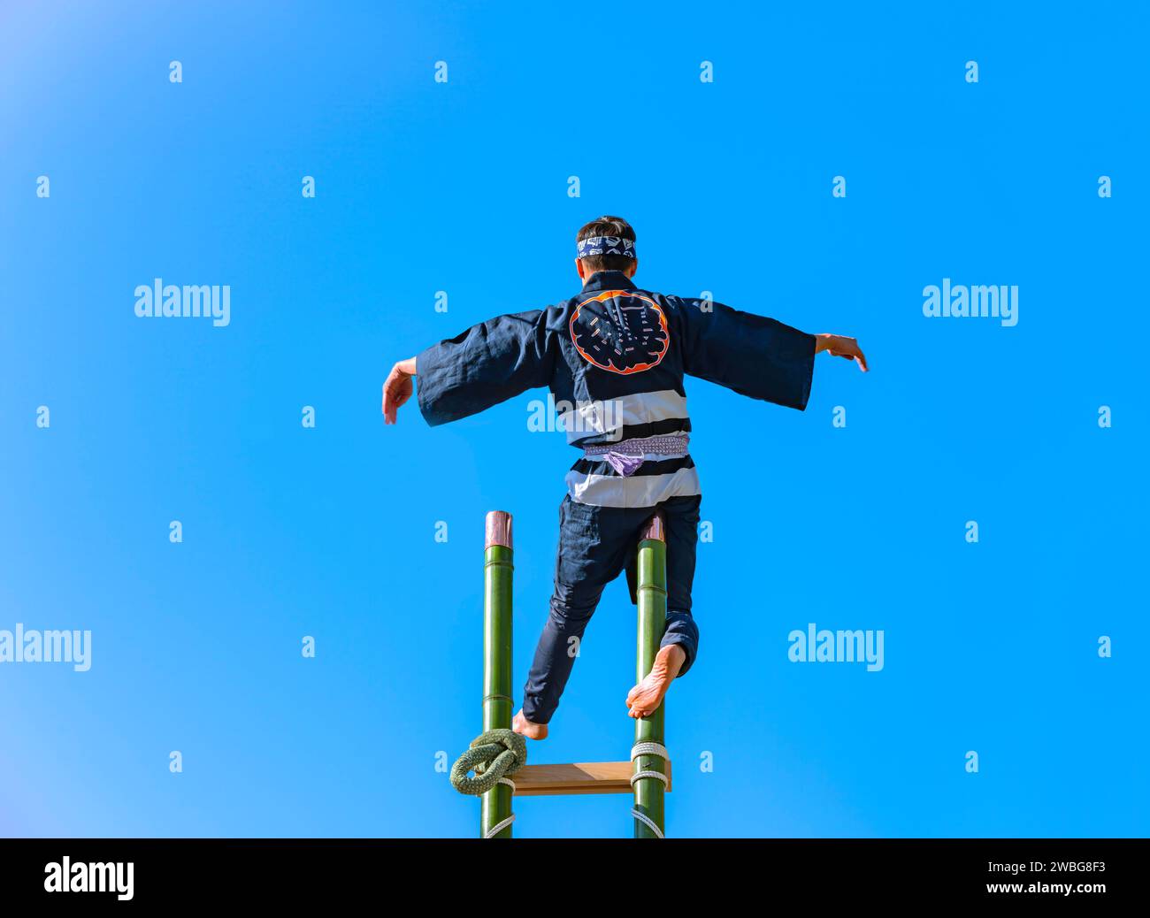 A Japanese hikeshi firefighter standing on one leg at the top of a tall ...