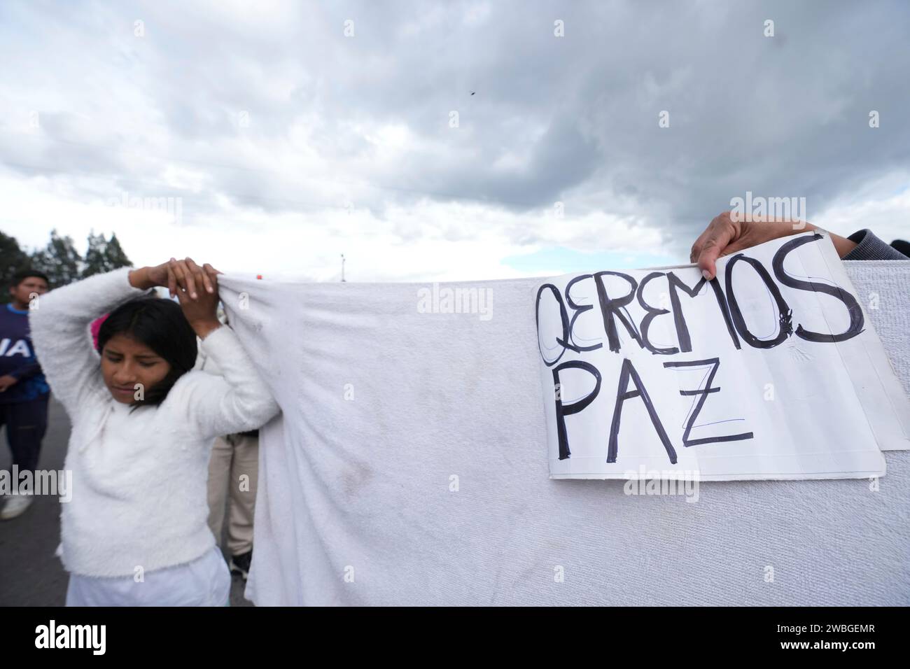 A relative of an inmate holds a sign asking for peace as a woman tries ...