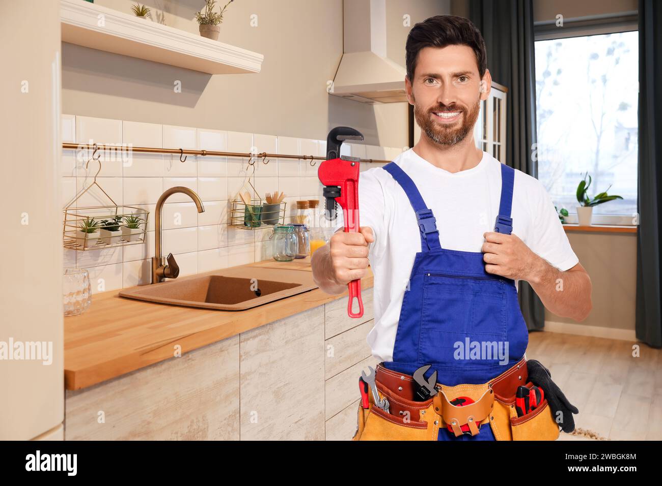 Plumber with pipe wrench and tool belt in kitchen, space for text Stock ...