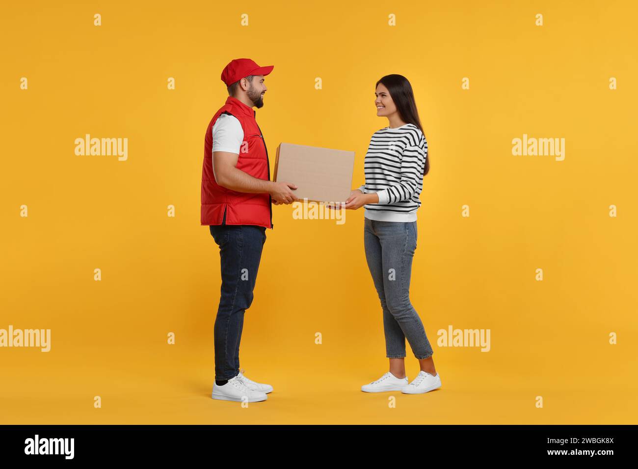 Smiling courier giving parcel to receiver on orange background Stock ...