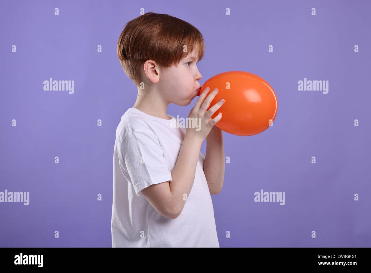 Boy inflating orange balloon on violet background Stock Photo - Alamy