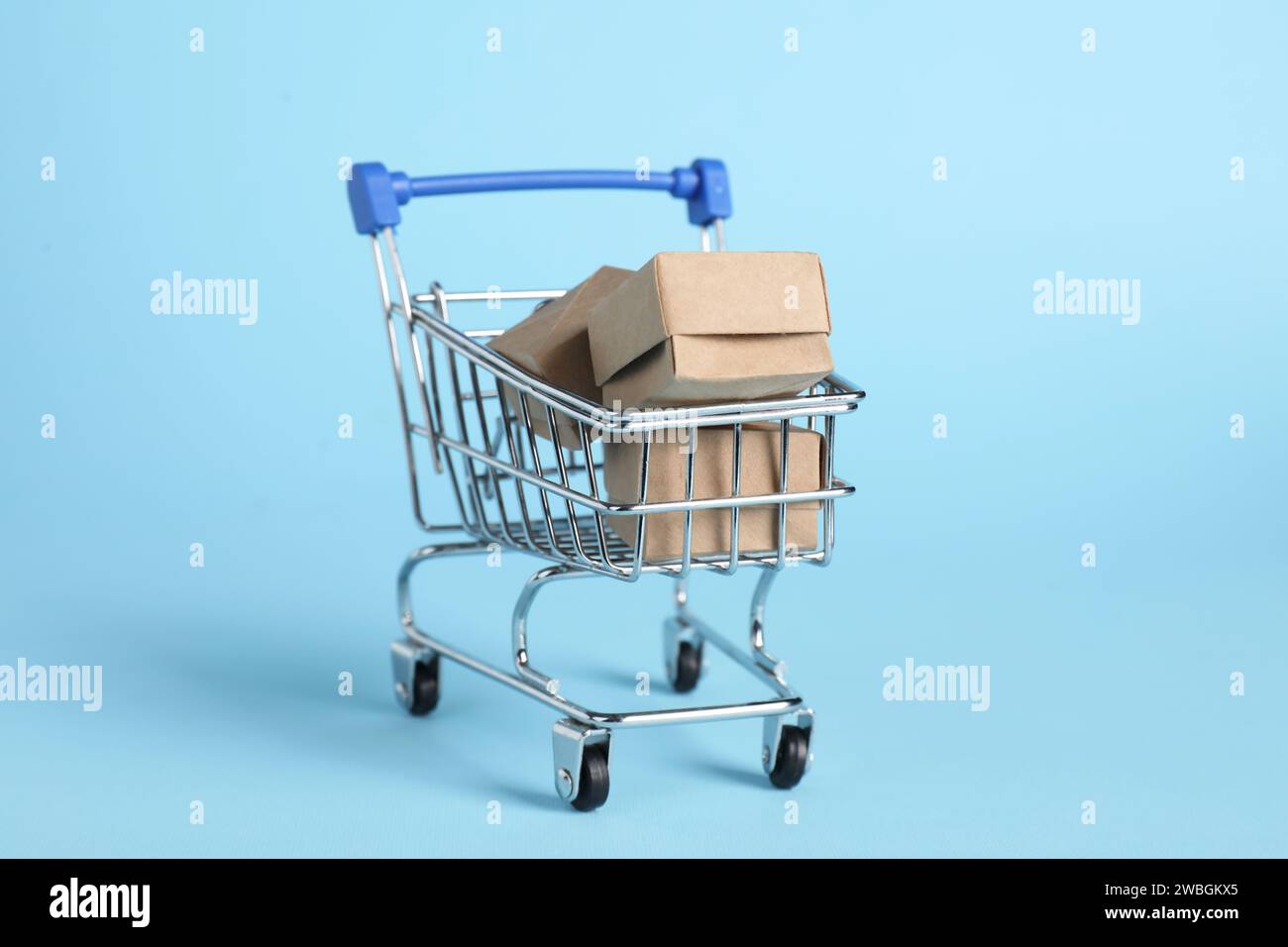 Small metal shopping cart with cardboard boxes on light blue background ...