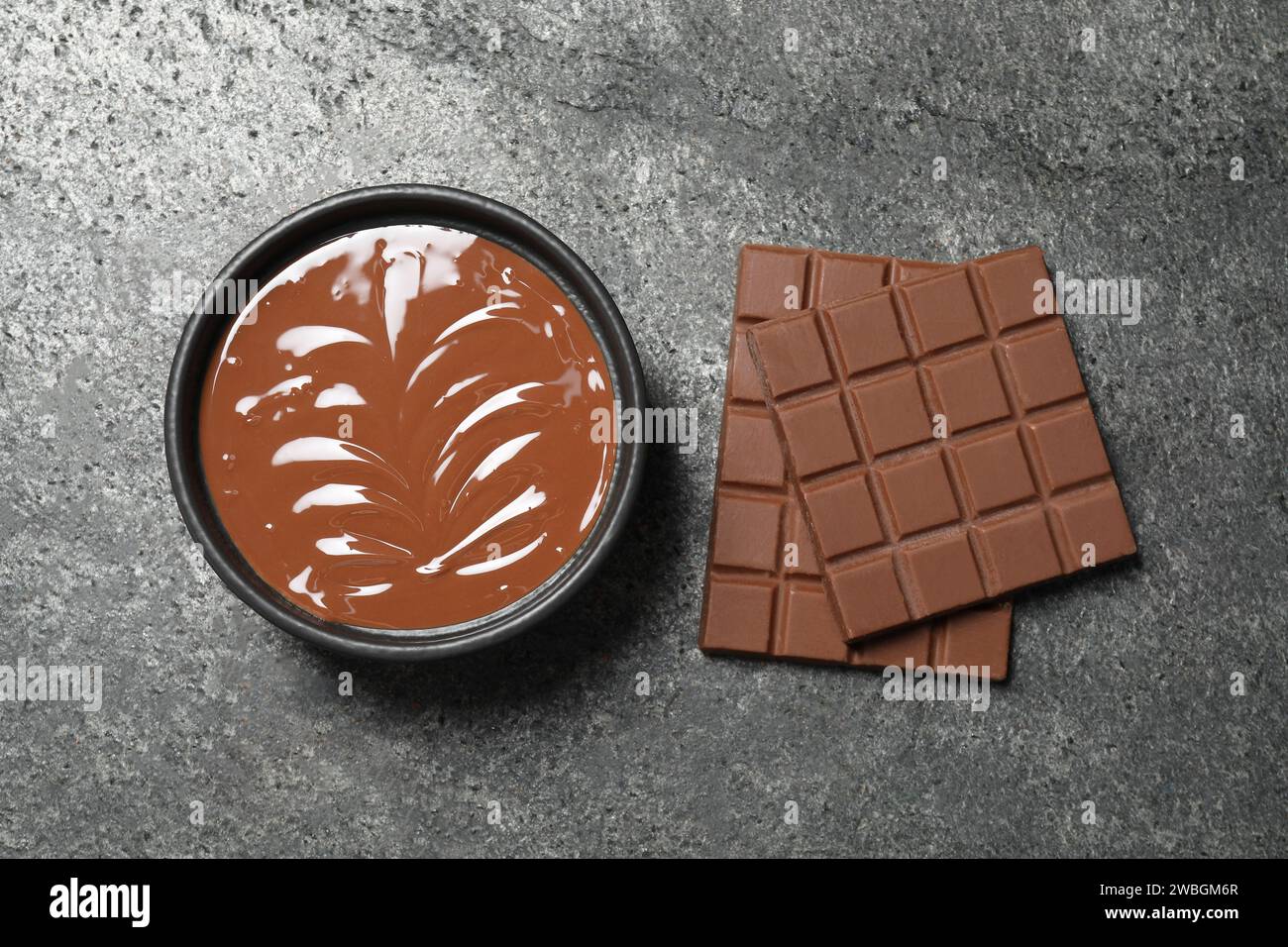 Tasty milk chocolate paste in bowl and bars on gray table, top view ...