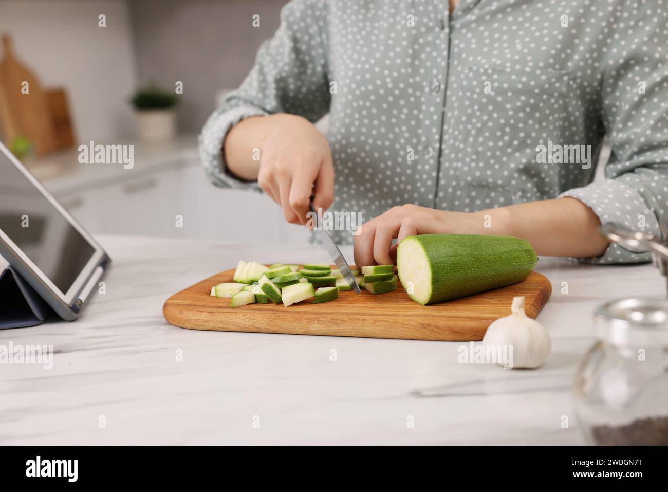 Cooking process. Woman cutting zucchini at white marble countertop ...