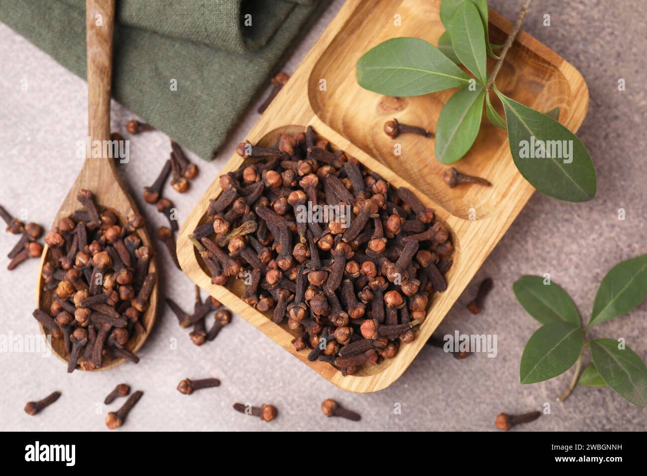 Wooden tray with aromatic cloves, spoon and green leaves on brown table ...