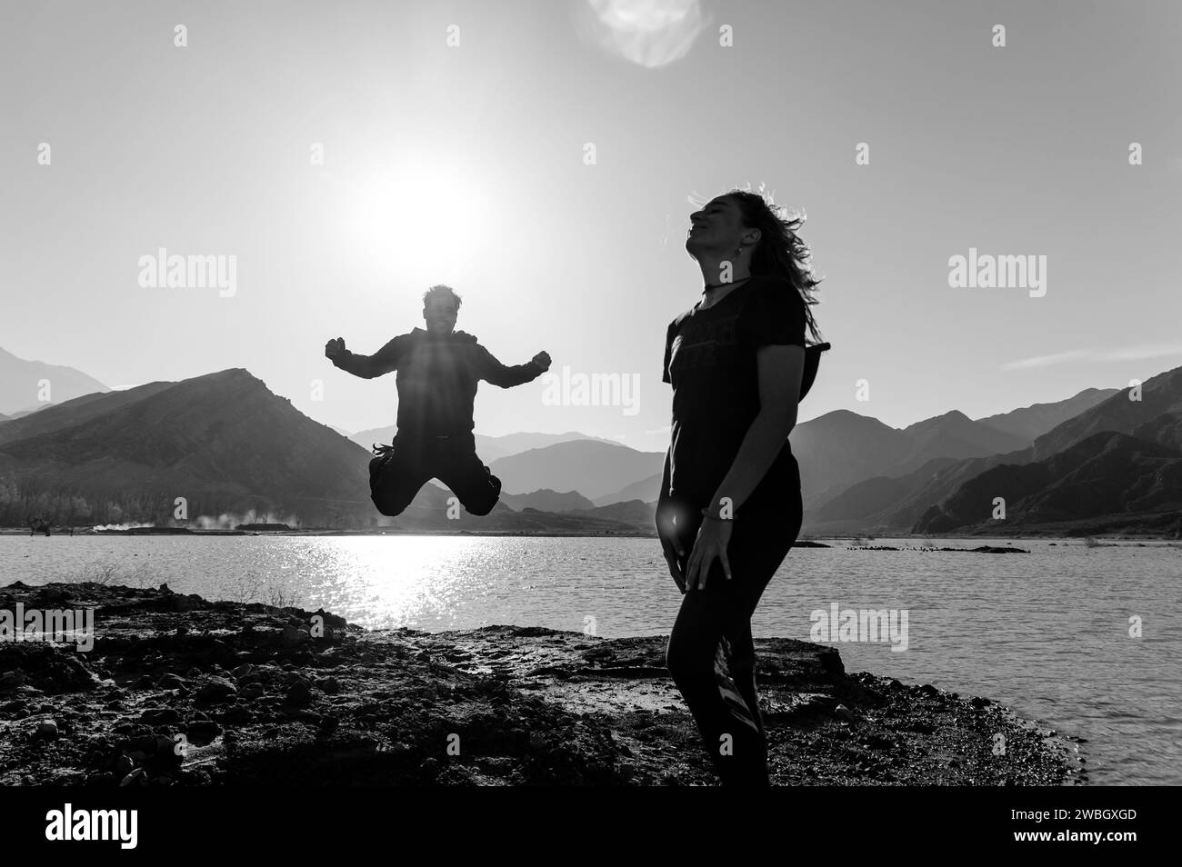 Couple jumping and enjoying a natural landscape of mountains and lake ...