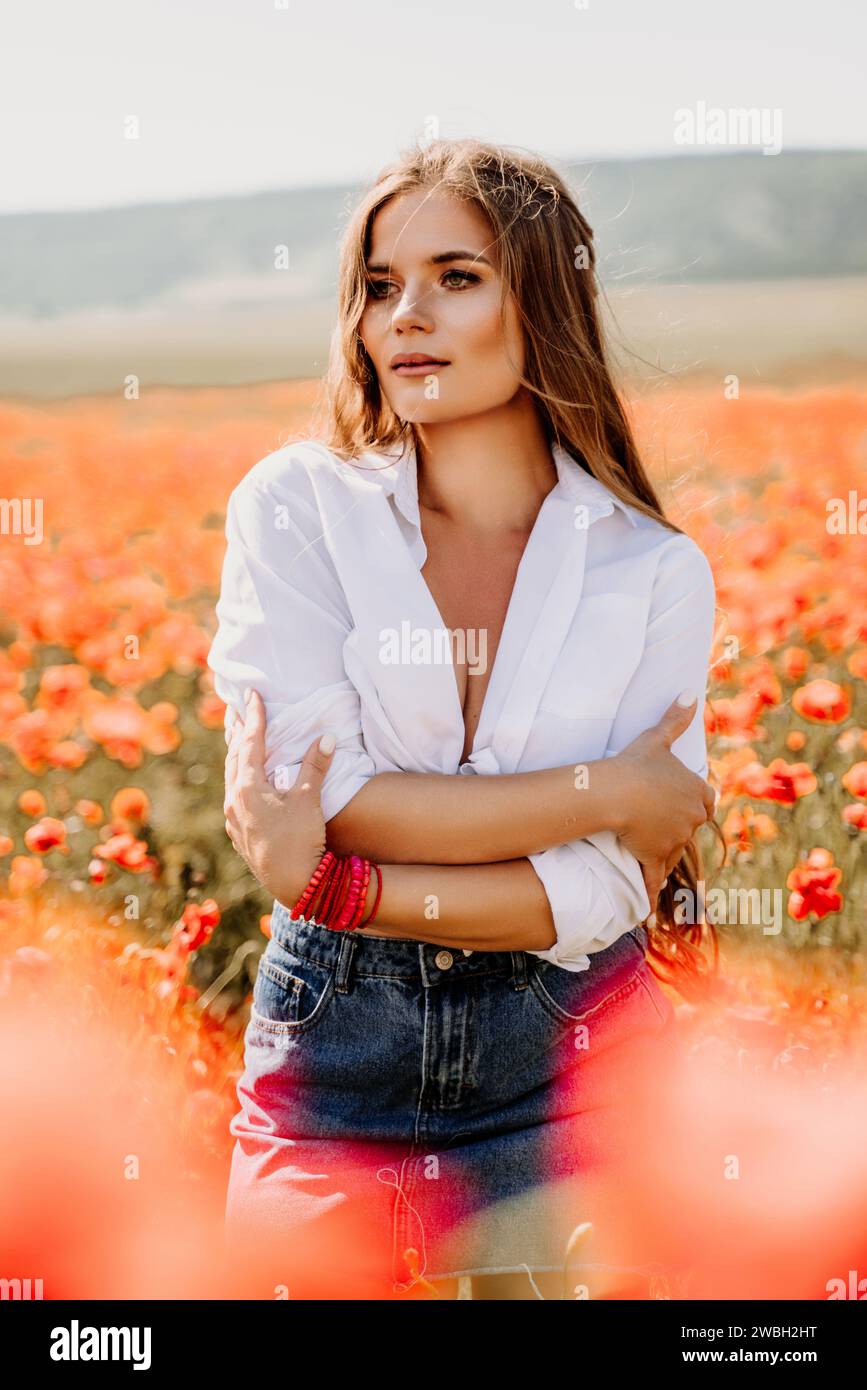 Happy woman in a poppy field in a white shirt and denim skirt with a ...
