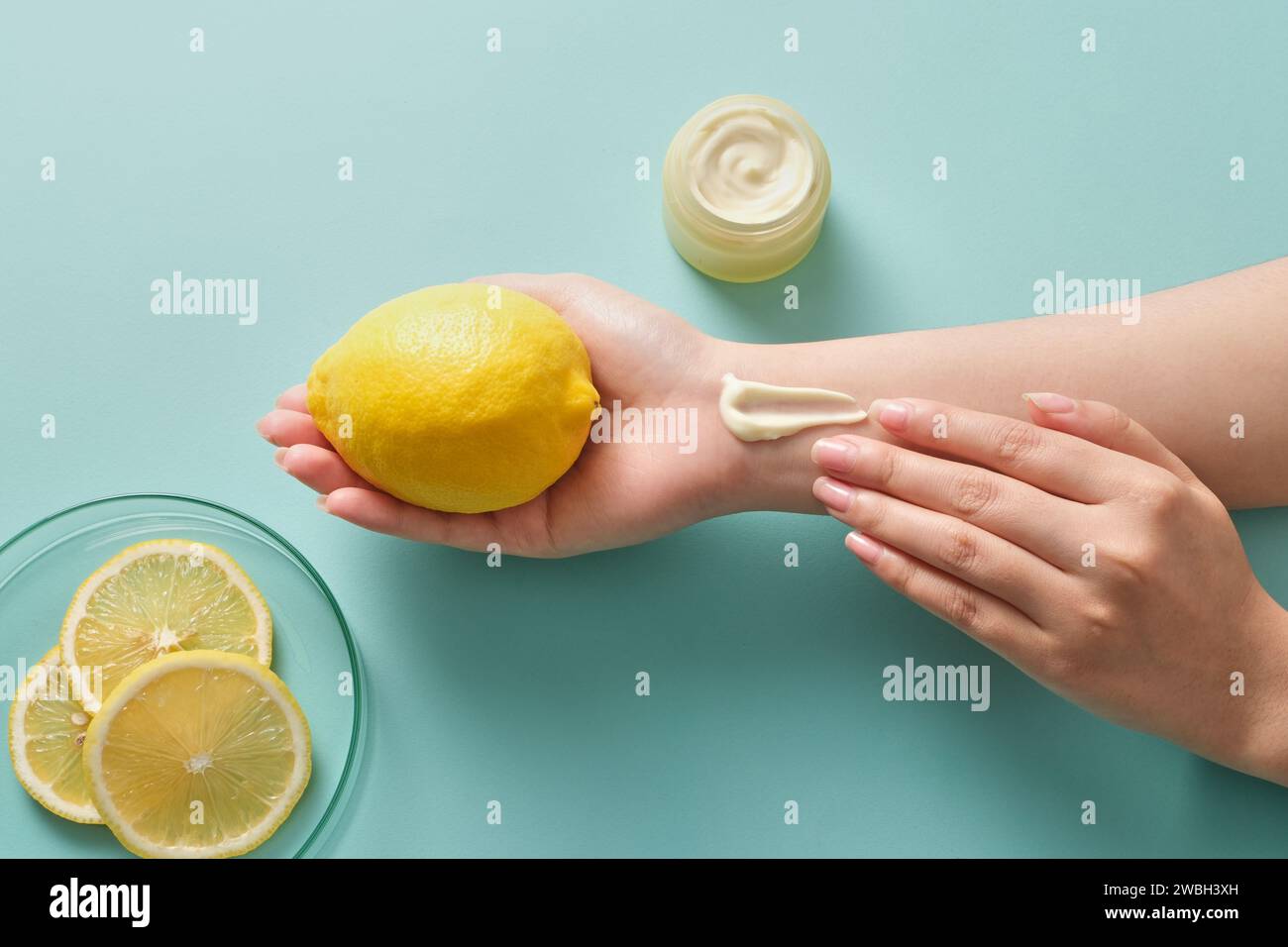 On a blue background, a fresh lemon on palm and the other hand applying ...