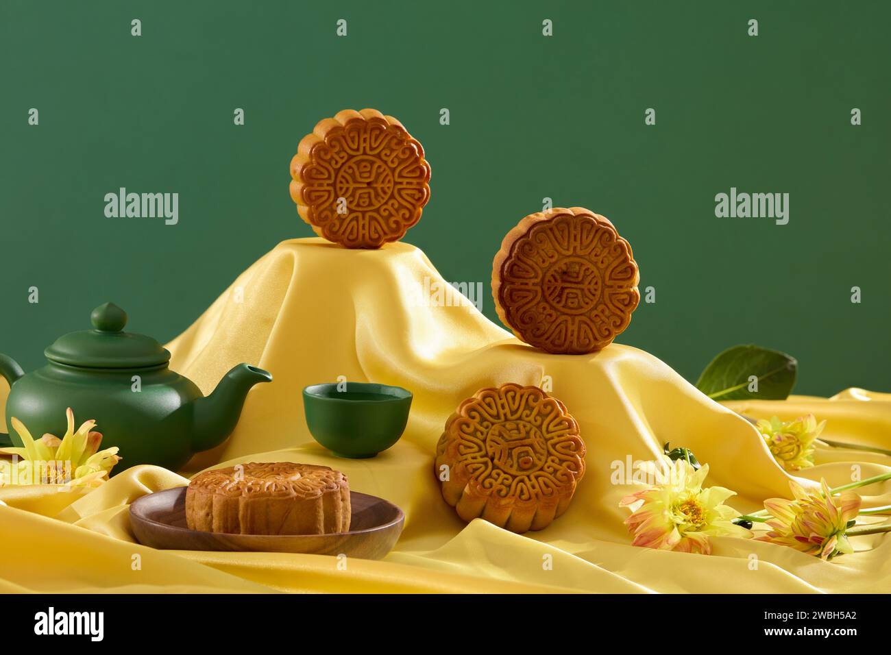 Round-shaped mooncakes placed on yellow fabric with a tea set in green color. Delicious Chinese ...