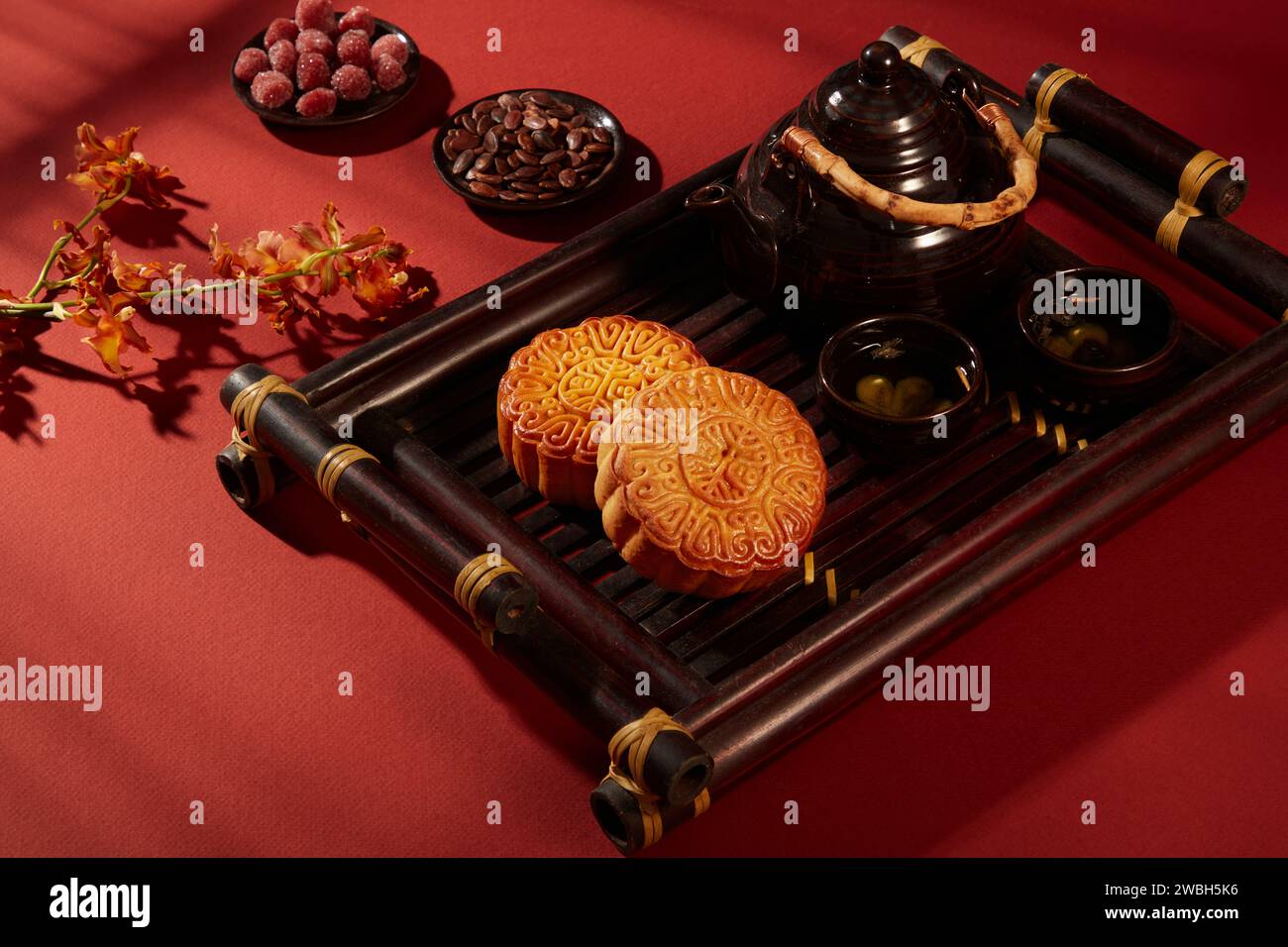 A tray featured two mooncakes and tea set arranged on red background ...