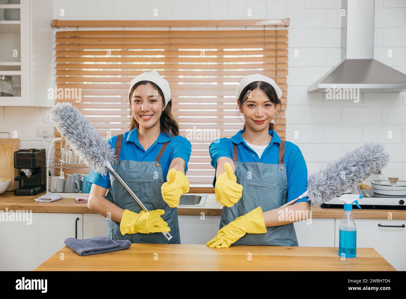 Two Asian cleaning service women on kitchen counter with duster foggy ...