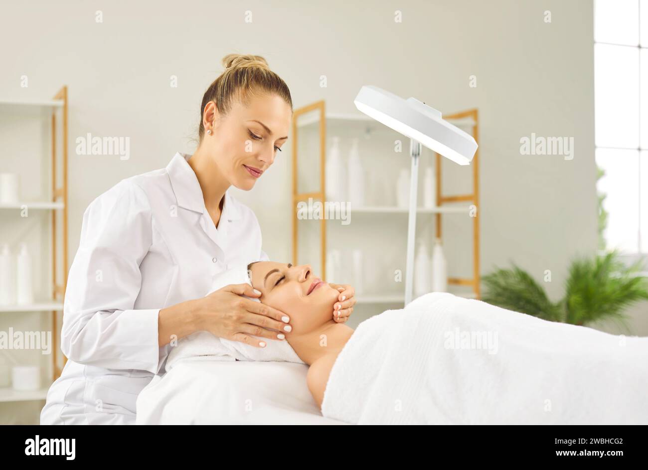 Young female cosmetologist examining woman client skin condition in ...