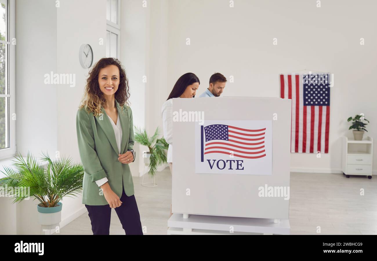 Voter woman looking at camera standing at vote center near voting booth ...