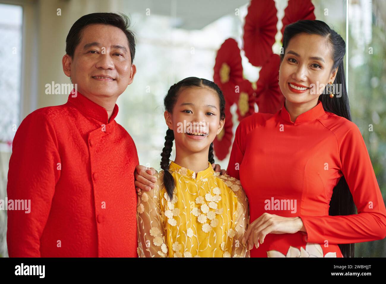 Cheerful Vietnamese mother, father and their teenage daughter wearing traditional dresses for ...