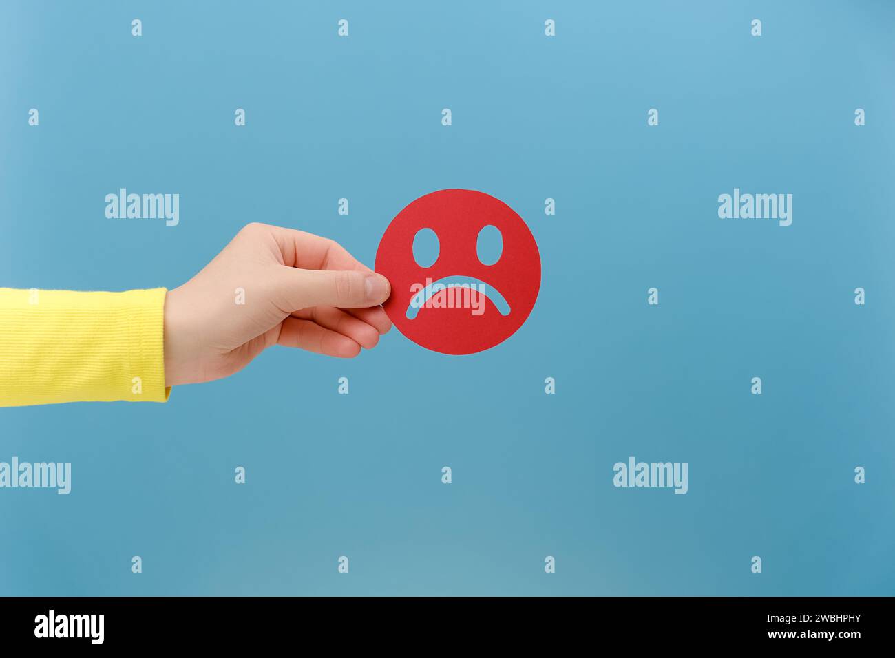 Close up of female hand holding round red sadness face paper emoticon ...