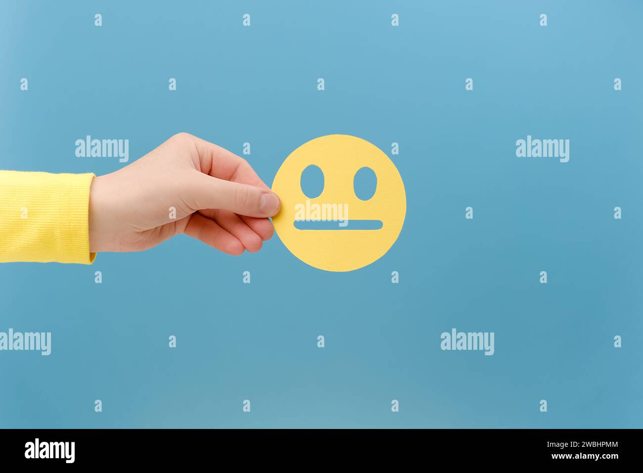 Close up of female hand holding yellow emoticon with boring face ...