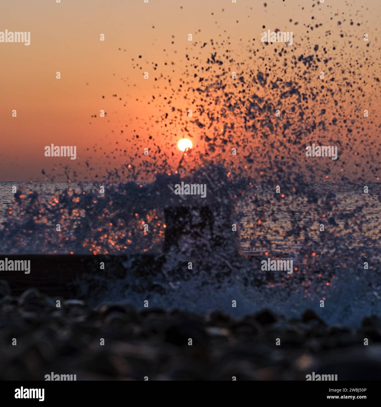 A bright orange sun rising behind a breaking wave sea on a Cold January ...