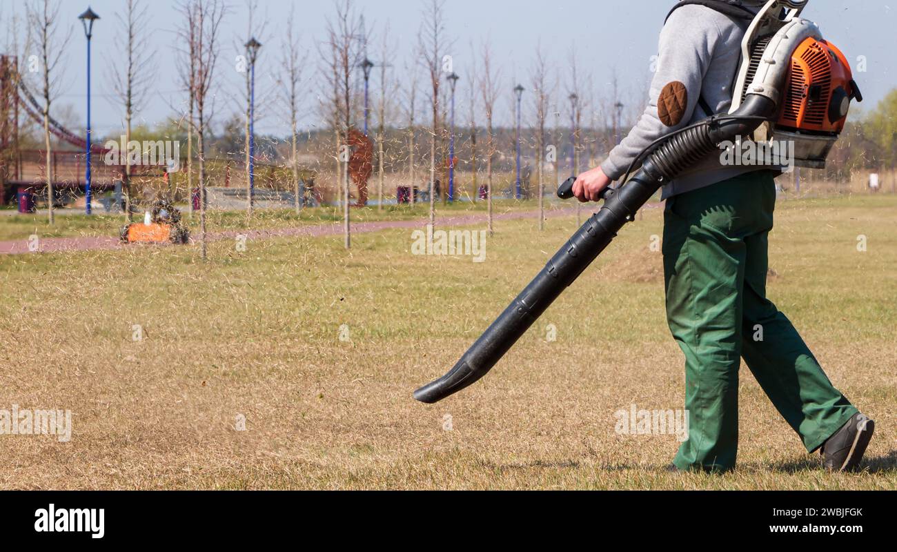 Gardener with air blower machine removes dry grass from the lawn in ...