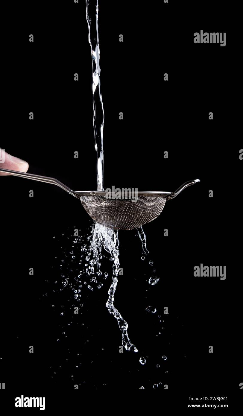 A stream of water pours through a small steel sieve in the hands of a ...