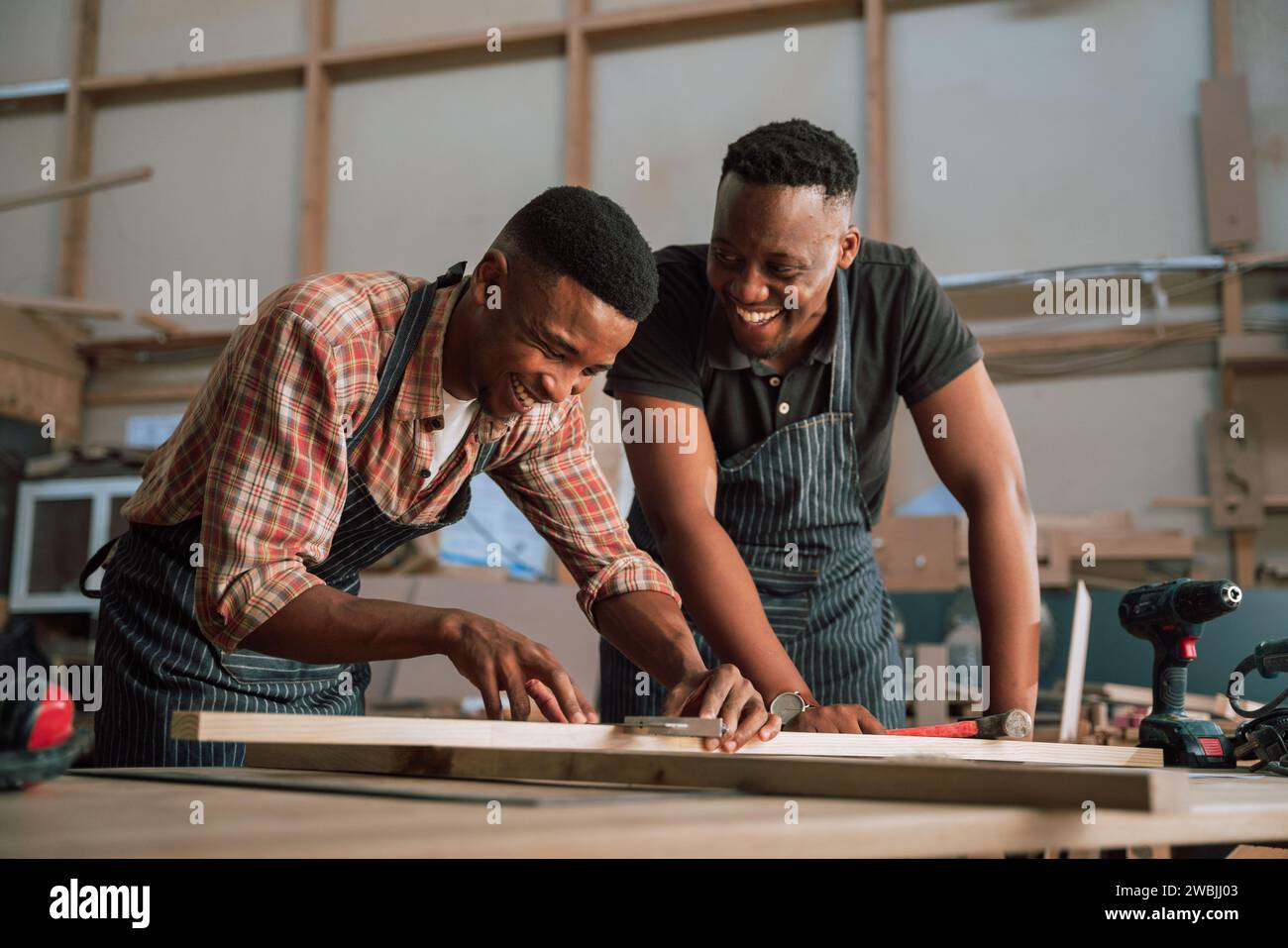African American male measures piece of wood as colleague assists him ...