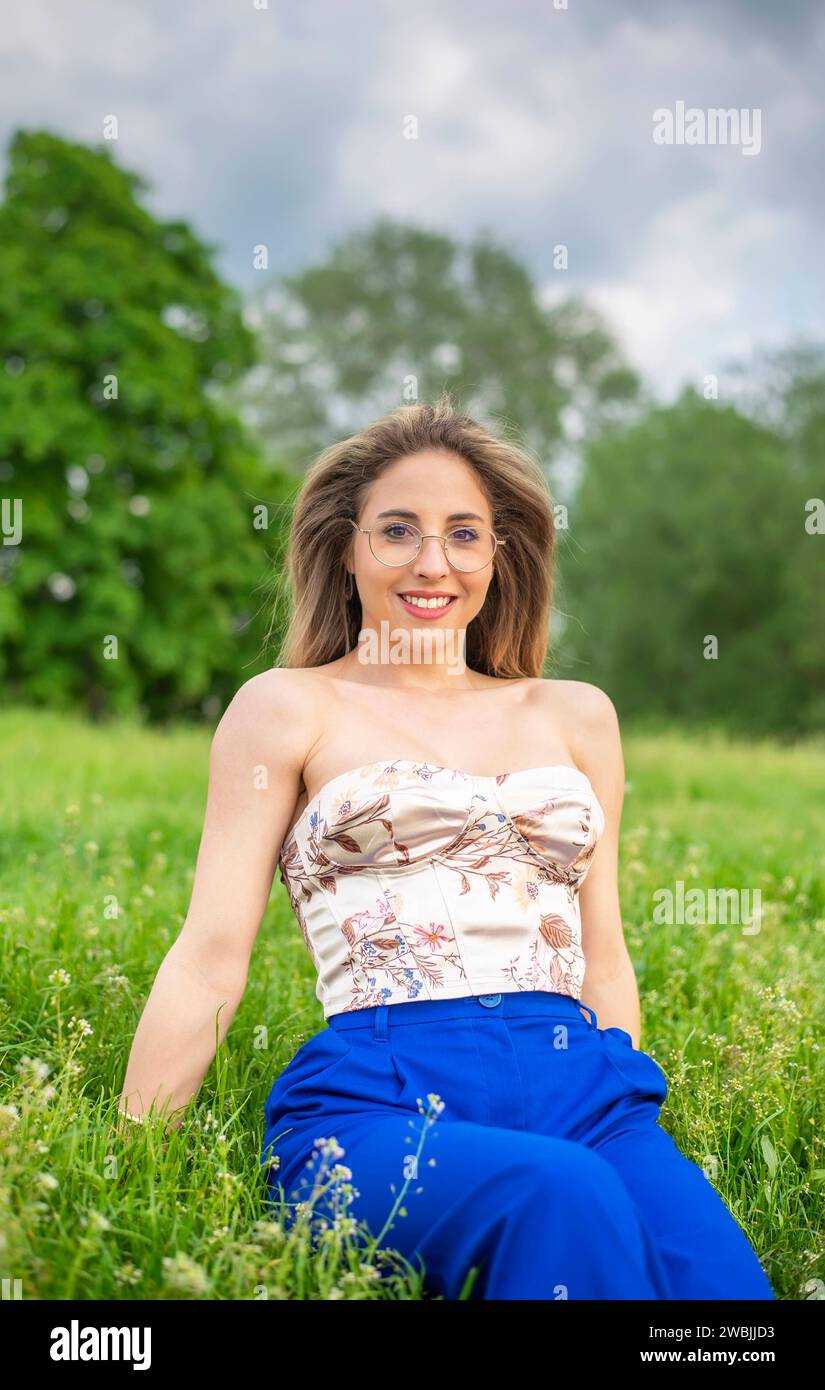 glückliche junge Frau mit Brille sitzt auf einer Wiese *** happy young ...