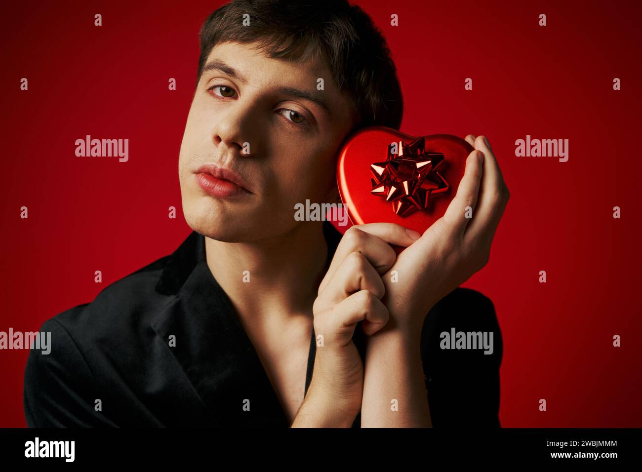 sentimental man in velvet blazer holding heart-shaped gift box on red ...