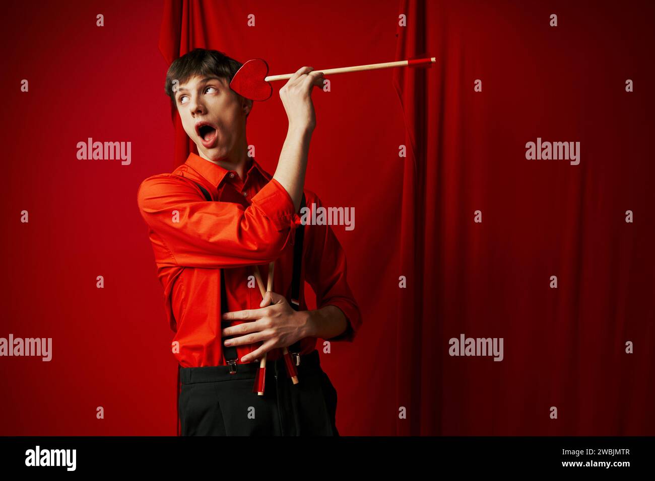 shocked young man with opened mouth holding heart shaped arrow on red ...