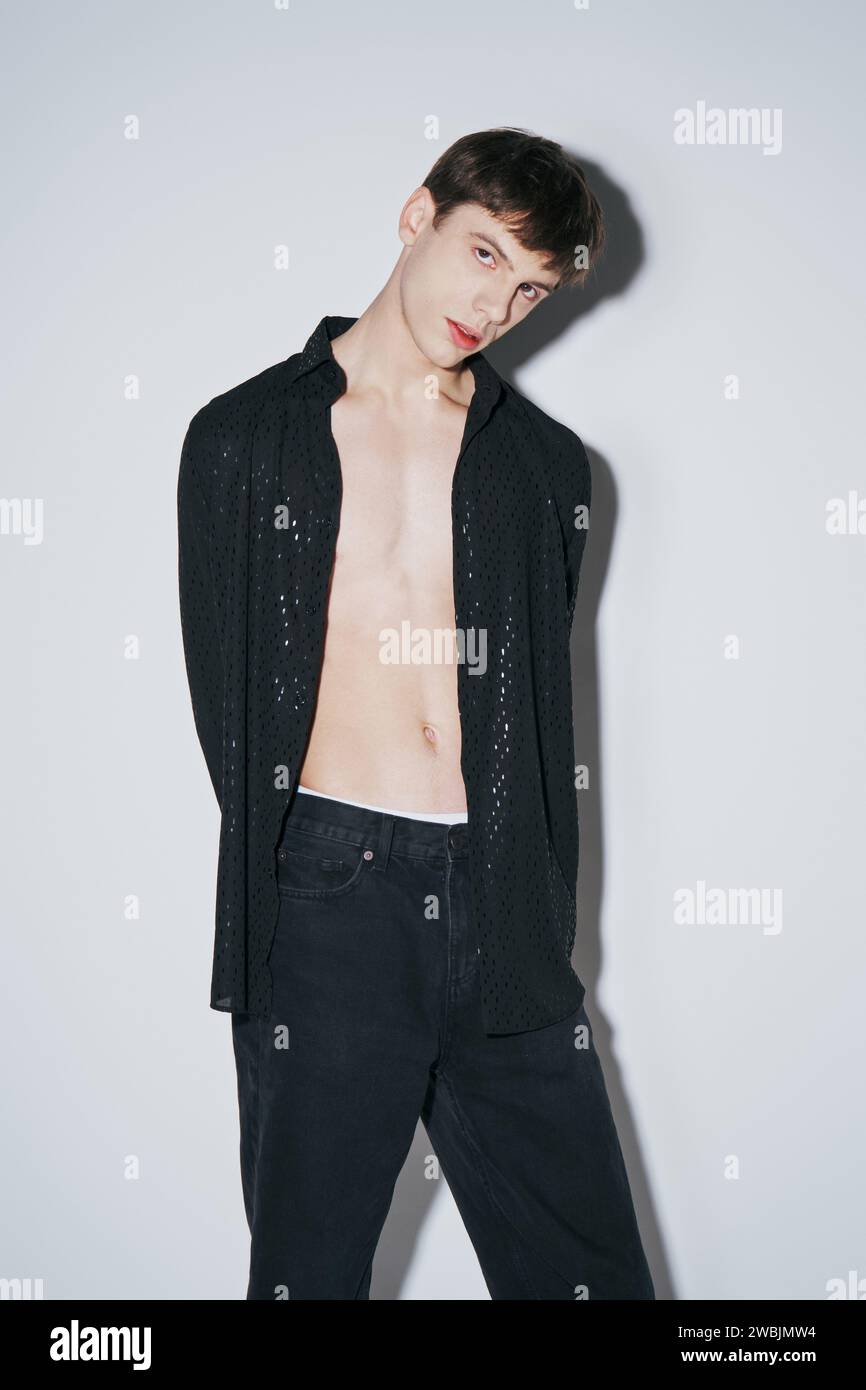 handsome young man in shiny black open shirt posing with hands behind ...