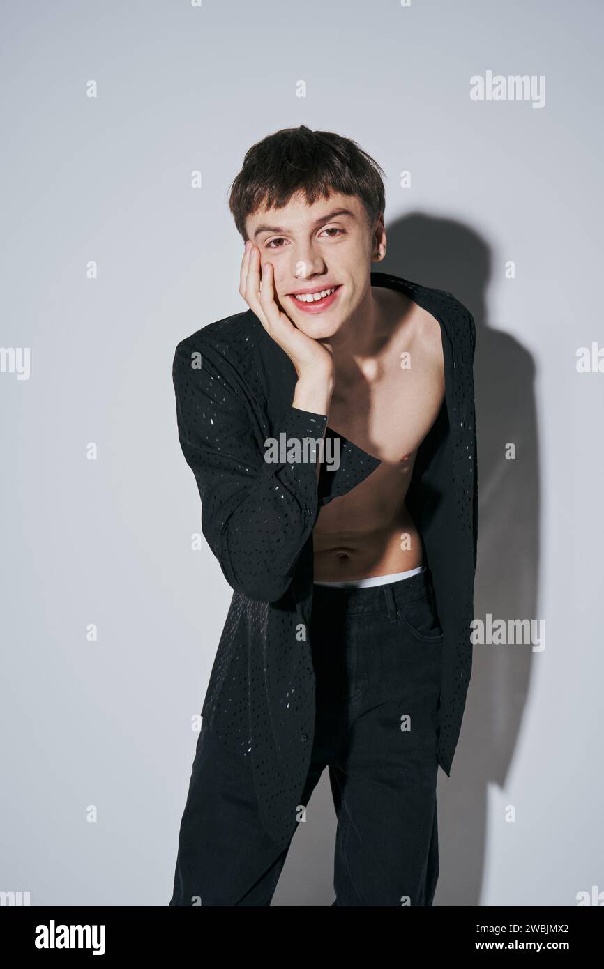 cheerful young man in dotted black shirt and jeans posing with hand ...