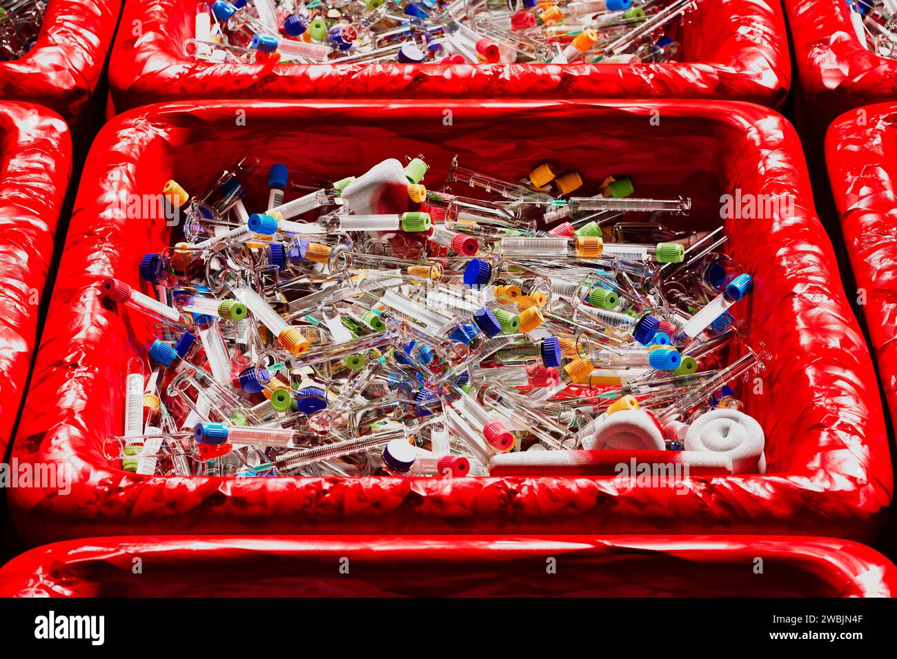 A red biohazard container overflows with discarded syringes, vials, and ...
