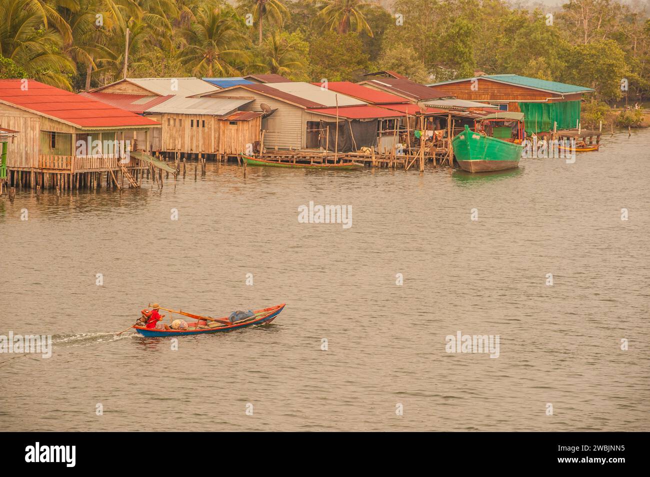 long tail boat passes riverside houses during the dry season, Southern ...