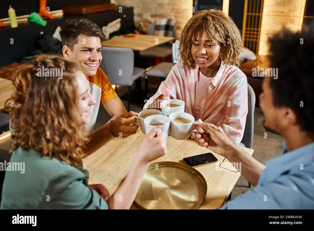 cheerful multicultural friends clinking coffee cups in lounge cafe of ...