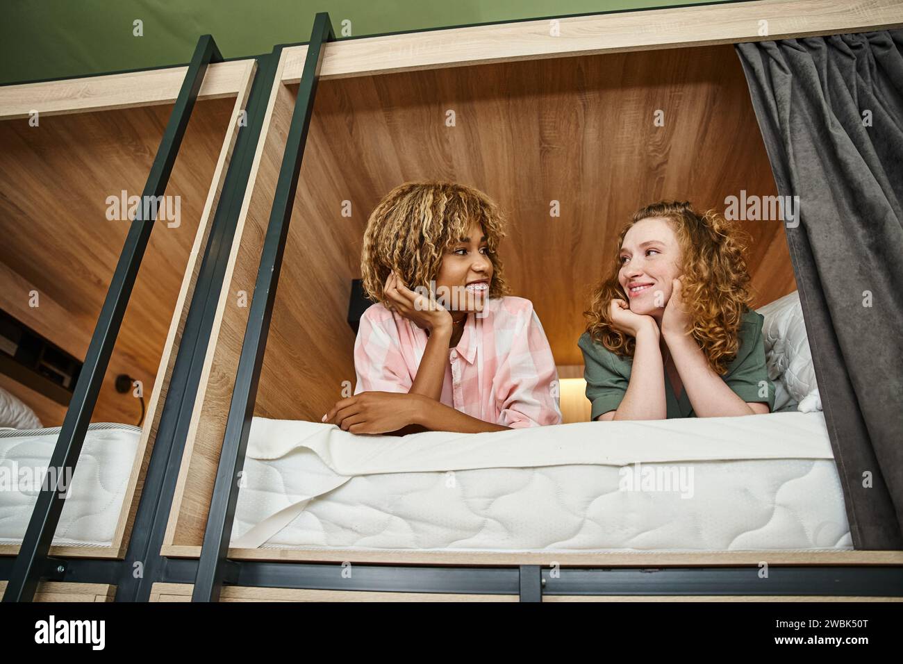 joyful multicultural girlfriends talking on double-decker bed in ...