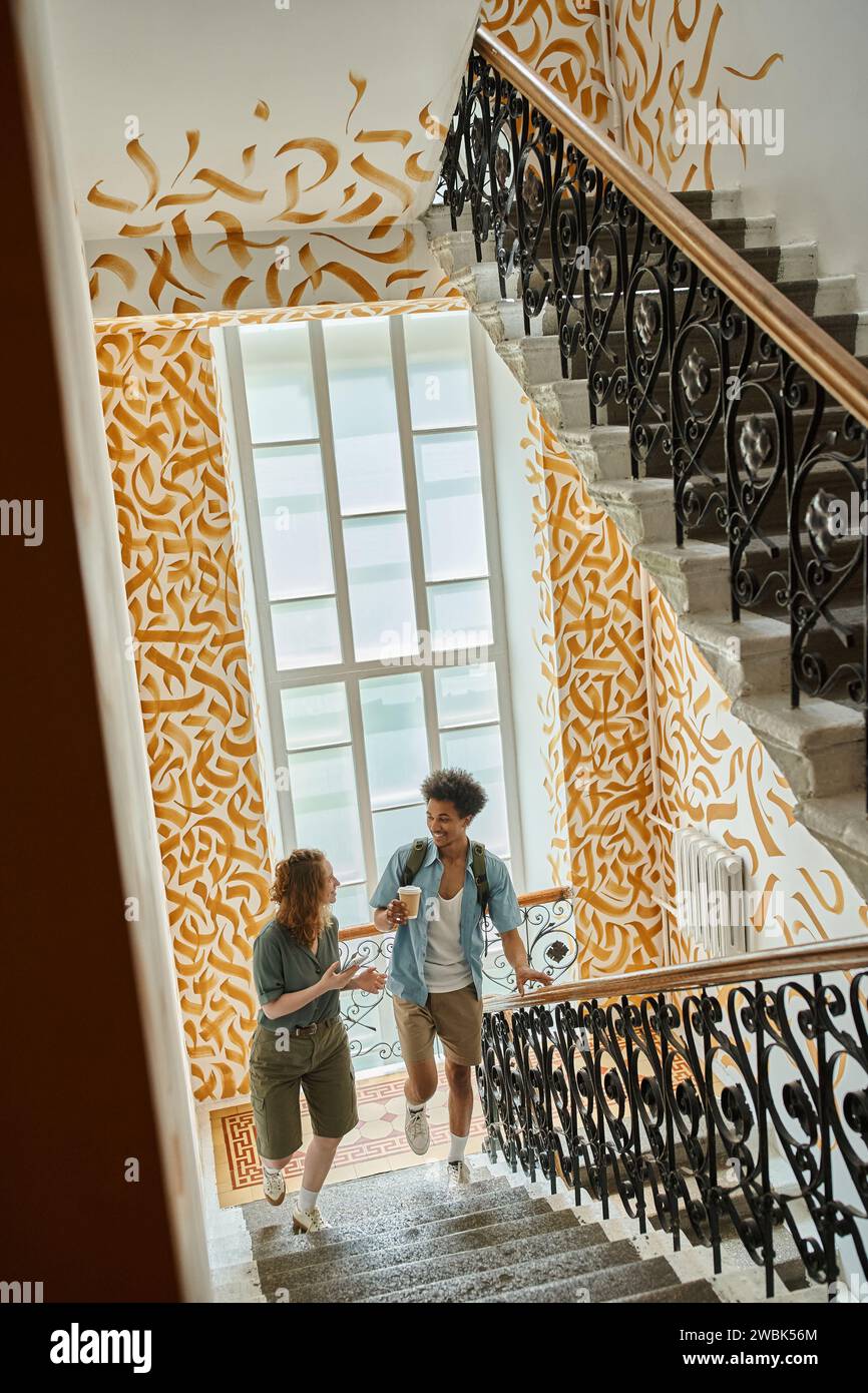happy multiethnic couple walking and talking on staircase with colorful ...