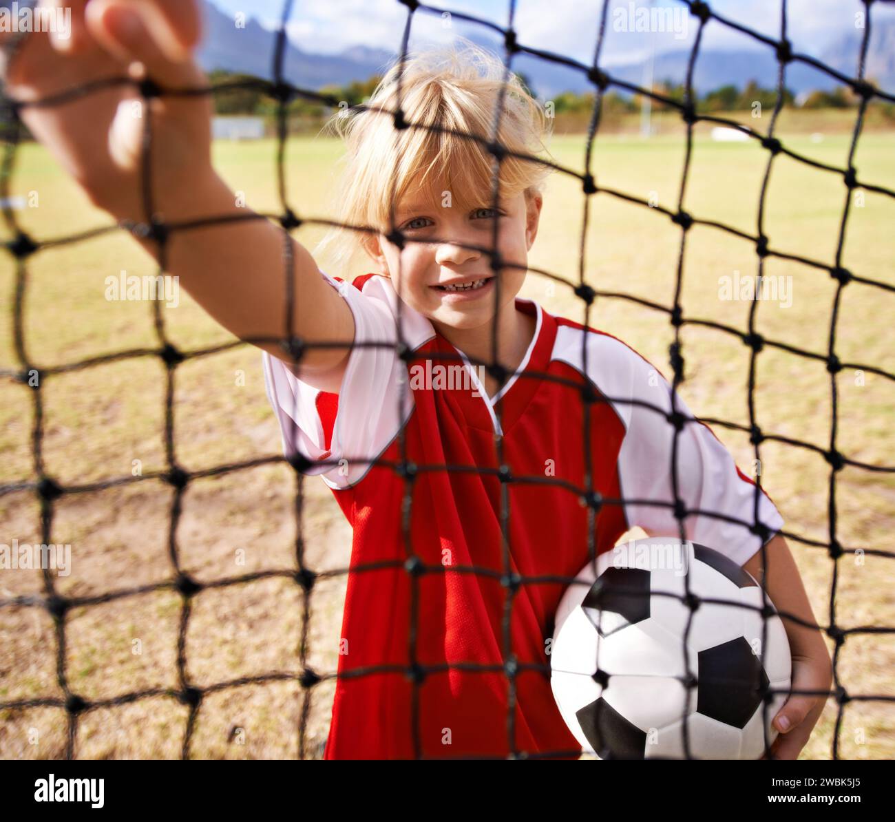 Little girl, soccer player and ball on goal net, smile and happy for ...