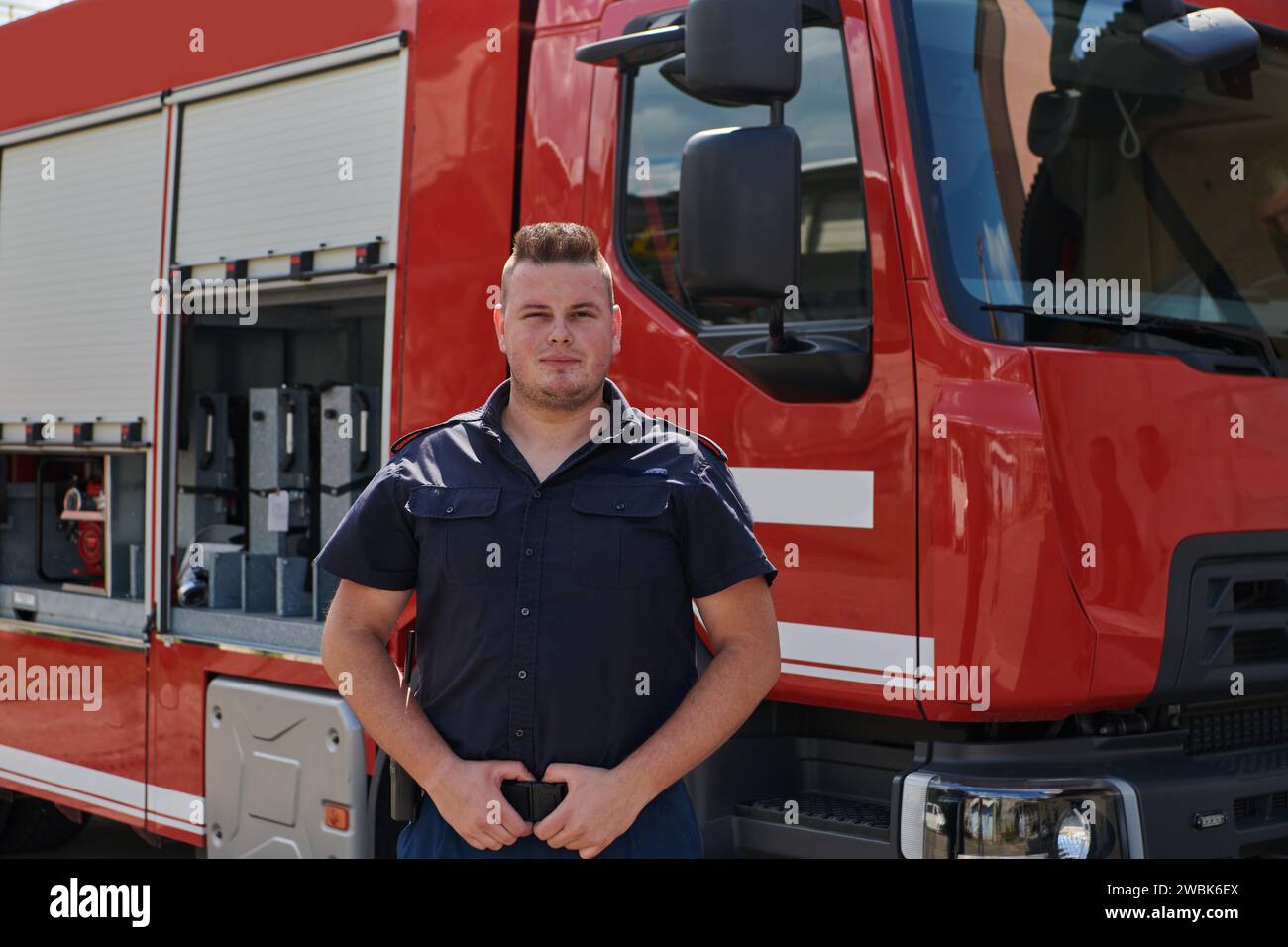 A confident firefighter strikes a pose in front of a modern firetruck ...