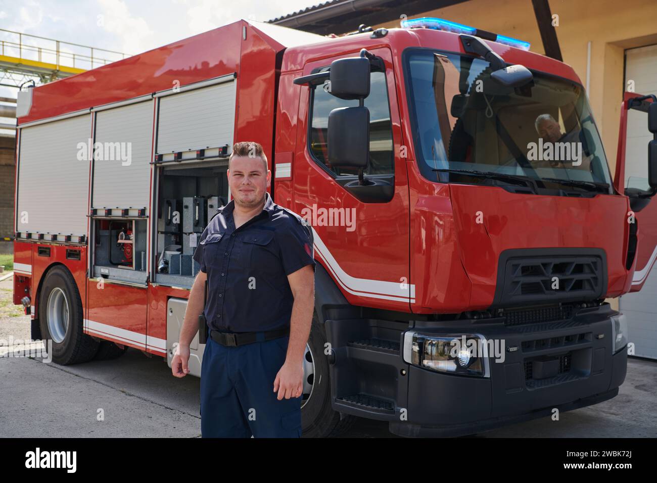 A confident firefighter strikes a pose in front of a modern firetruck ...