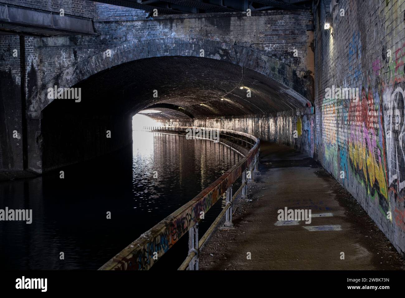 Graffiti along the long curved brickwork tunnel underneath train lines ...