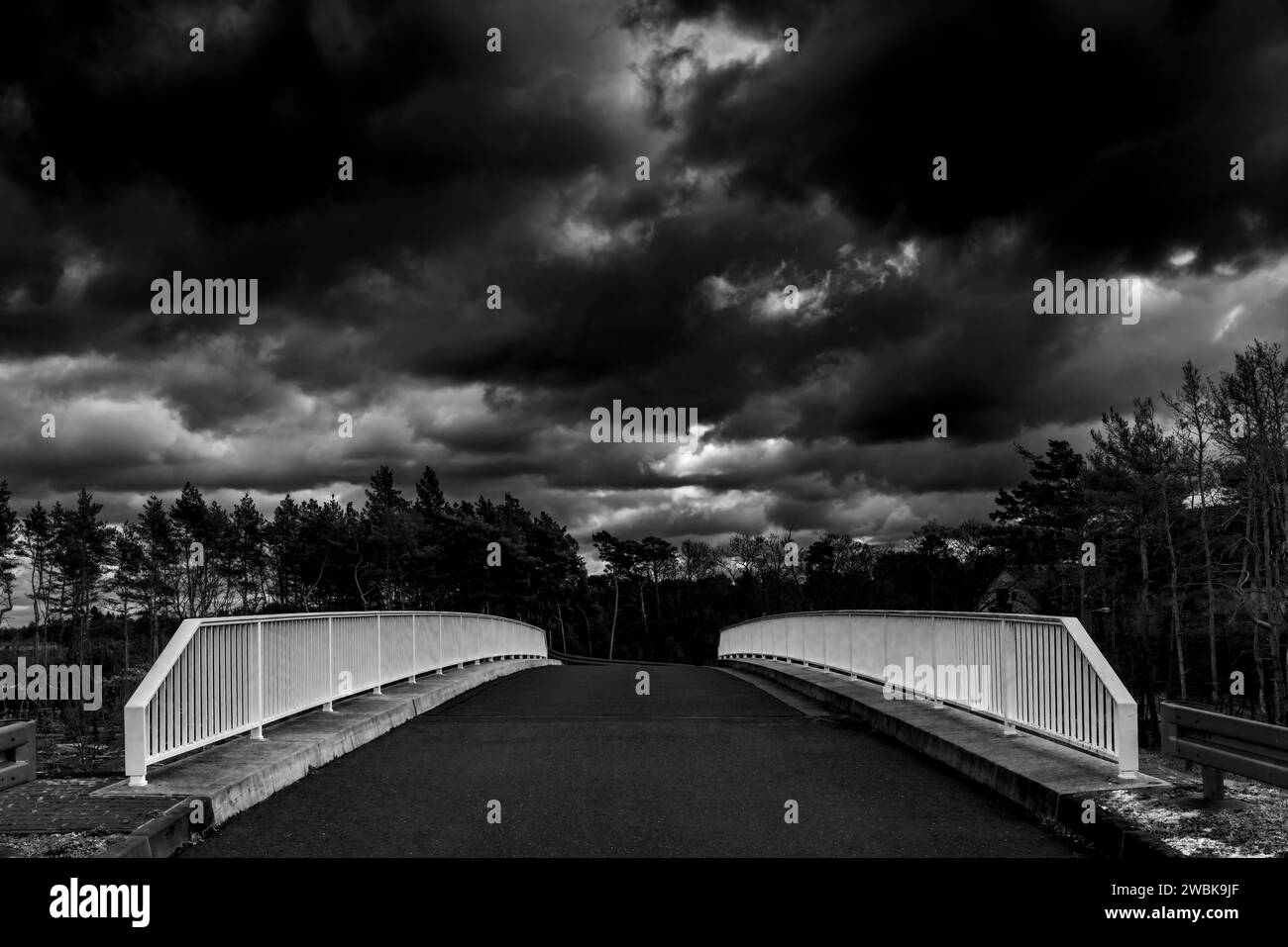 Country road that leads over a bridge, iron railings, sky full of rain ...