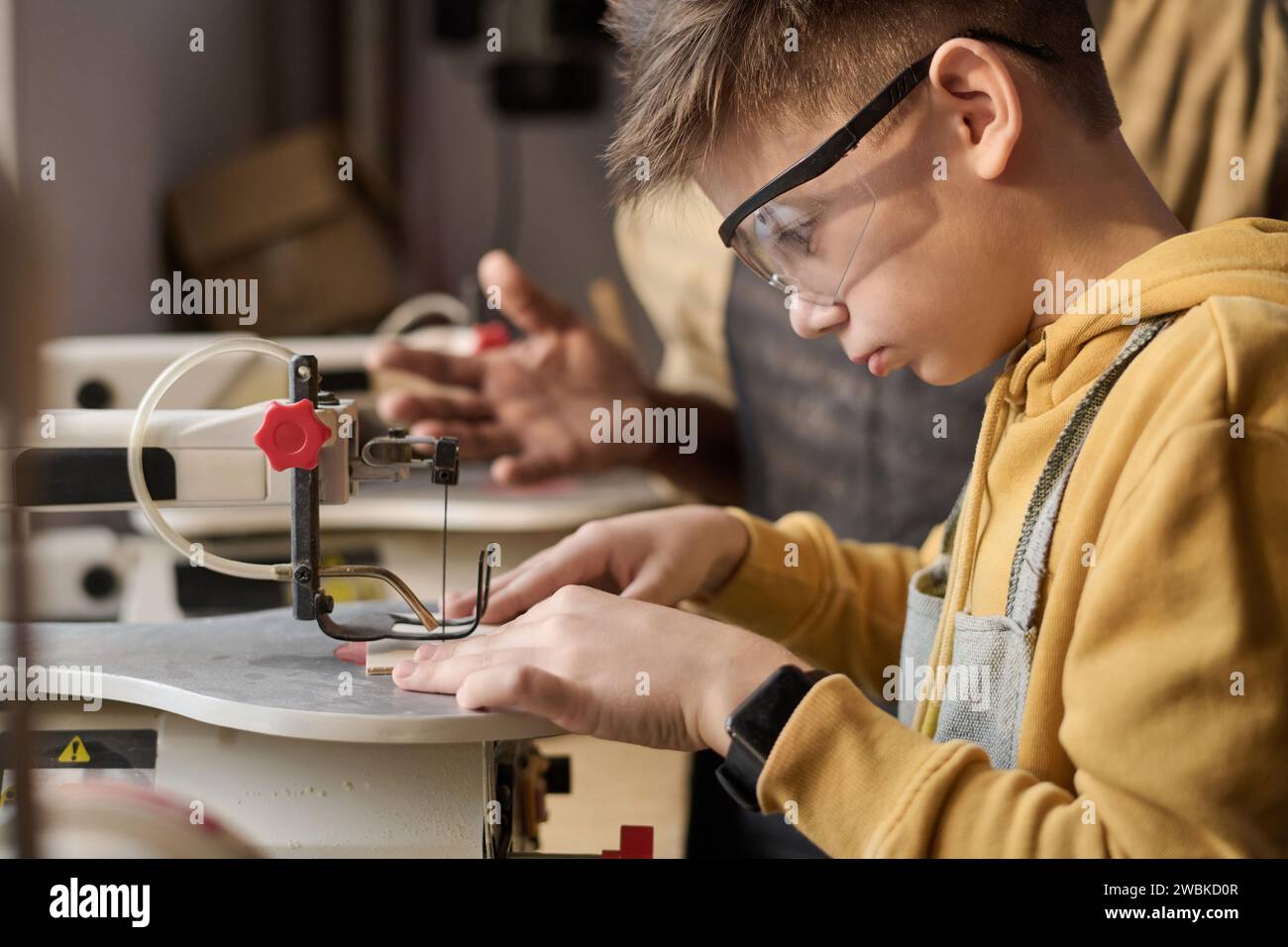 Side view portrait of focused Caucasian boy cutting wood using machine ...