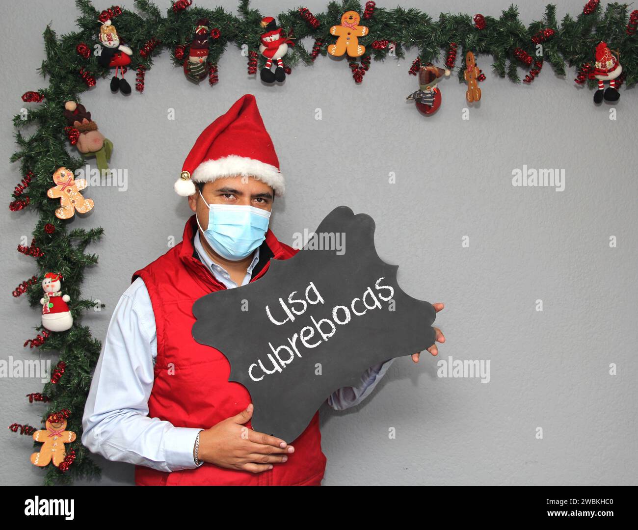 Latin man with protection mask, Santa hat and blackboard with message ...