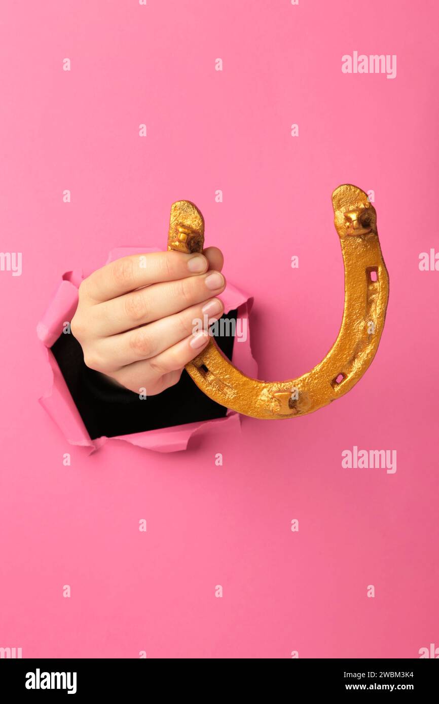 Female hand with golden horseshoe punching through the pink paper. Top ...