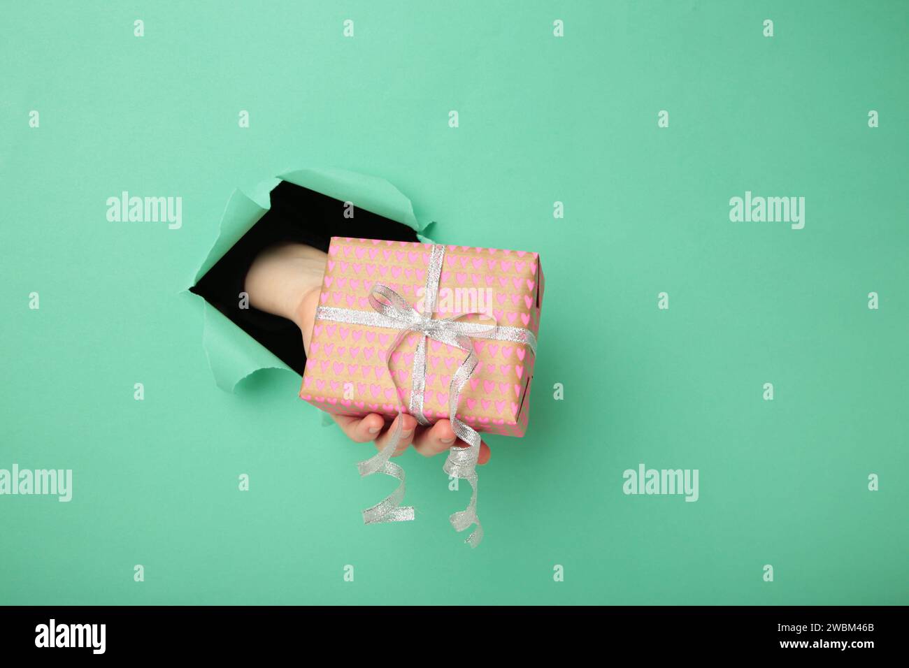 Female hand with gift box punching through the mint paper. Top view ...