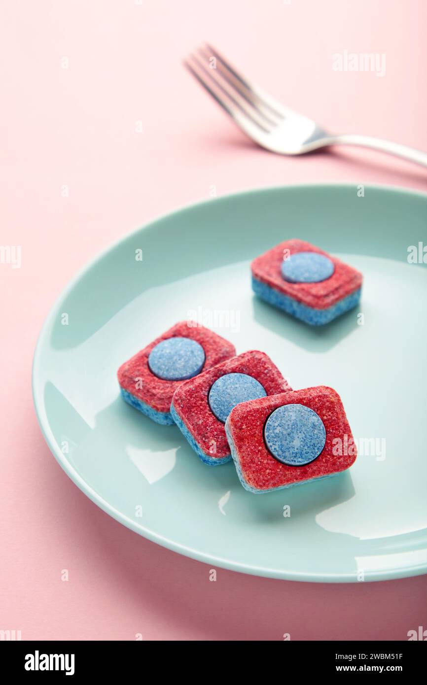 Dishwasher detergent tablet with fork and dishes on pink background ...