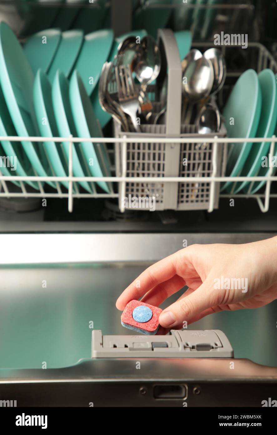 Dishwasher tablet in hand on the background of an open dishwasher. Top ...