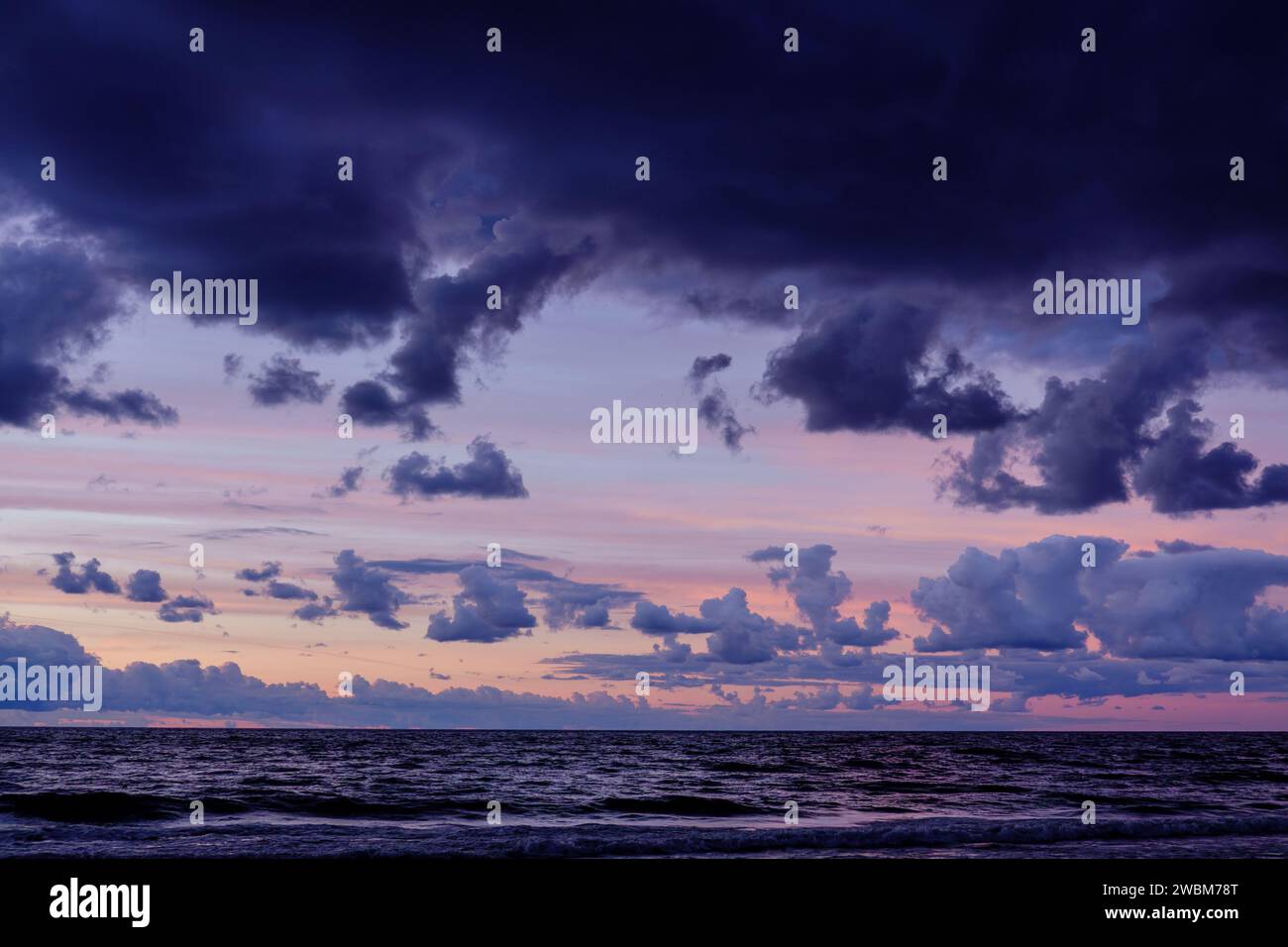 Twilight seascape with layered clouds, radiant sunset hues casting over ...