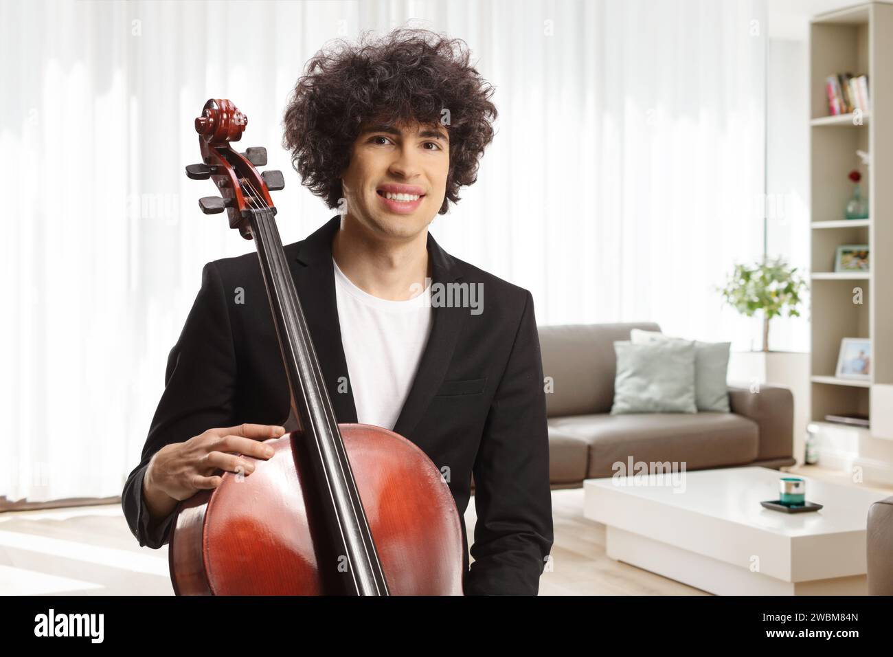 Portrait of a young male artist with a cello posing at home in a living ...
