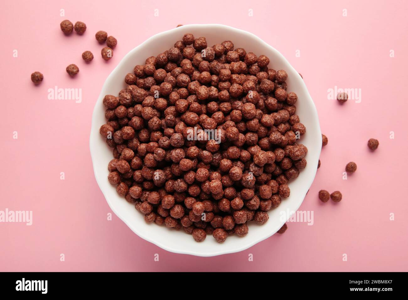 Chocolate cereal corn balls in a white bowl on a pink background. Top ...